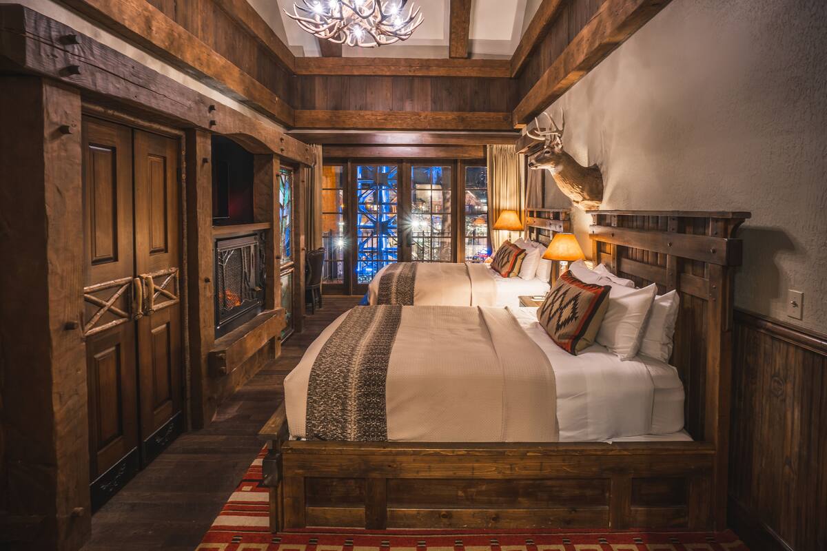 Quarto de madeira com uma cama grande, uma lareira e um cabeça de veado na parede.