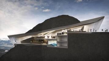 Um edifício moderno com arquitetura marcante, teto inclinado e vários níveis, situado em meio a uma paisagem montanhosa.
