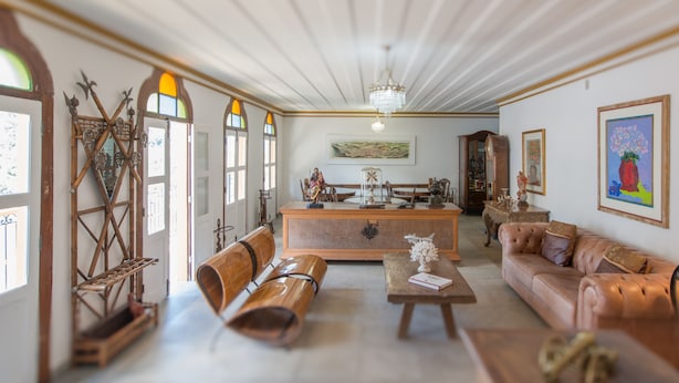 Uma sala de estar espaçosa com um banco de madeira, um sofá e uma mesa de centro. Há um candelabro pendurado no teto e um quadro na parede.