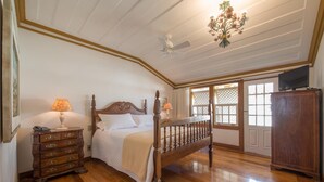 Quarto com cama de madeira, mesa de cabeceira, cômoda, televisão e ventilador de teto.