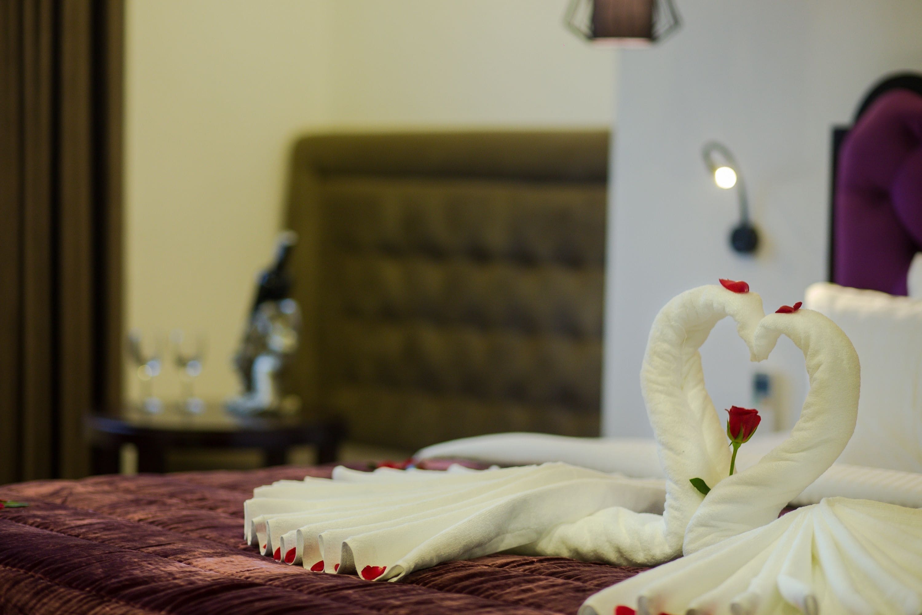 Uma cama com colcha vermelha e um cisne decorativo feito de toalhas, com uma rosa.