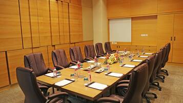 Uma sala de conferência com uma mesa comprida, cadeiras de couro marrom, garrafas de água e uma tela de projetor.