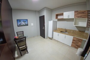 Cozinha compacta com armários brancos, bancada de madeira e um espaço de refeições com cadeira e mesa.