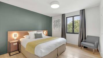 Quarto de hotel moderno com cama grande, mesa de cabeceira e uma cadeira.