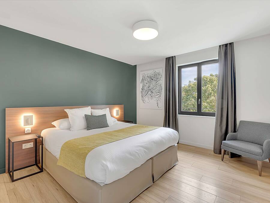 Quarto de hotel moderno com cama grande, mesa de cabeceira e uma cadeira.