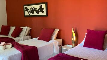 Quarto de hotel com duas camas, roupa de cama vermelha e branca, unidade de ar condicionado, obra de arte na parede e abajur.