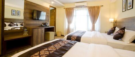 Quarto de hotel com duas camas, televisão, escrivaninha e espelho.