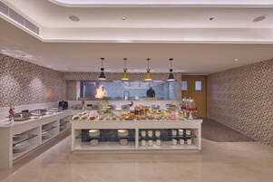 Buffet moderno com diversos alimentos e bebidas, um chef trabalhando e um design de parede estampado.
