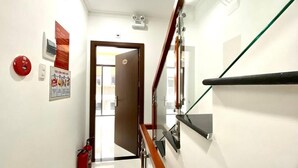 Um corredor moderno de hotel com escada de madeira, um extintor de incêndio e uma porta que dá para outro quarto.