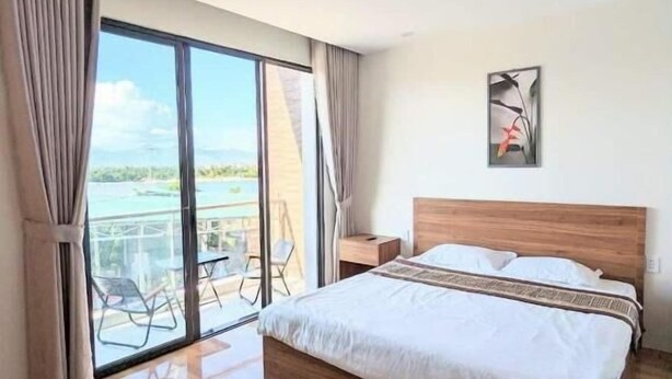 Quarto de hotel com uma cama grande, vista para o exterior e varanda com cadeiras.