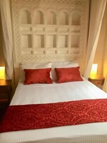 Uma cama com cabeceira branca, duas almofadas vermelhas e um edredom vermelho.