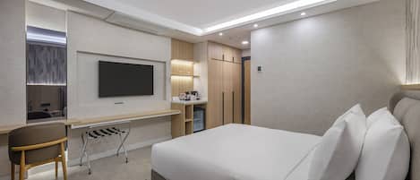 Quarto de hotel com cama, escrivaninha, cadeira, televisão, minibar e guarda-roupa.
