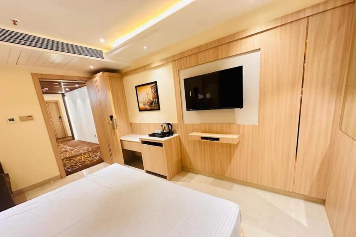 Quarto de hotel com cama, escrivaninha, televisão na parede e um quadro.
