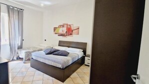Quarto com cama, mesa de cabeceira, cortinas na janela e um quadro na parede.