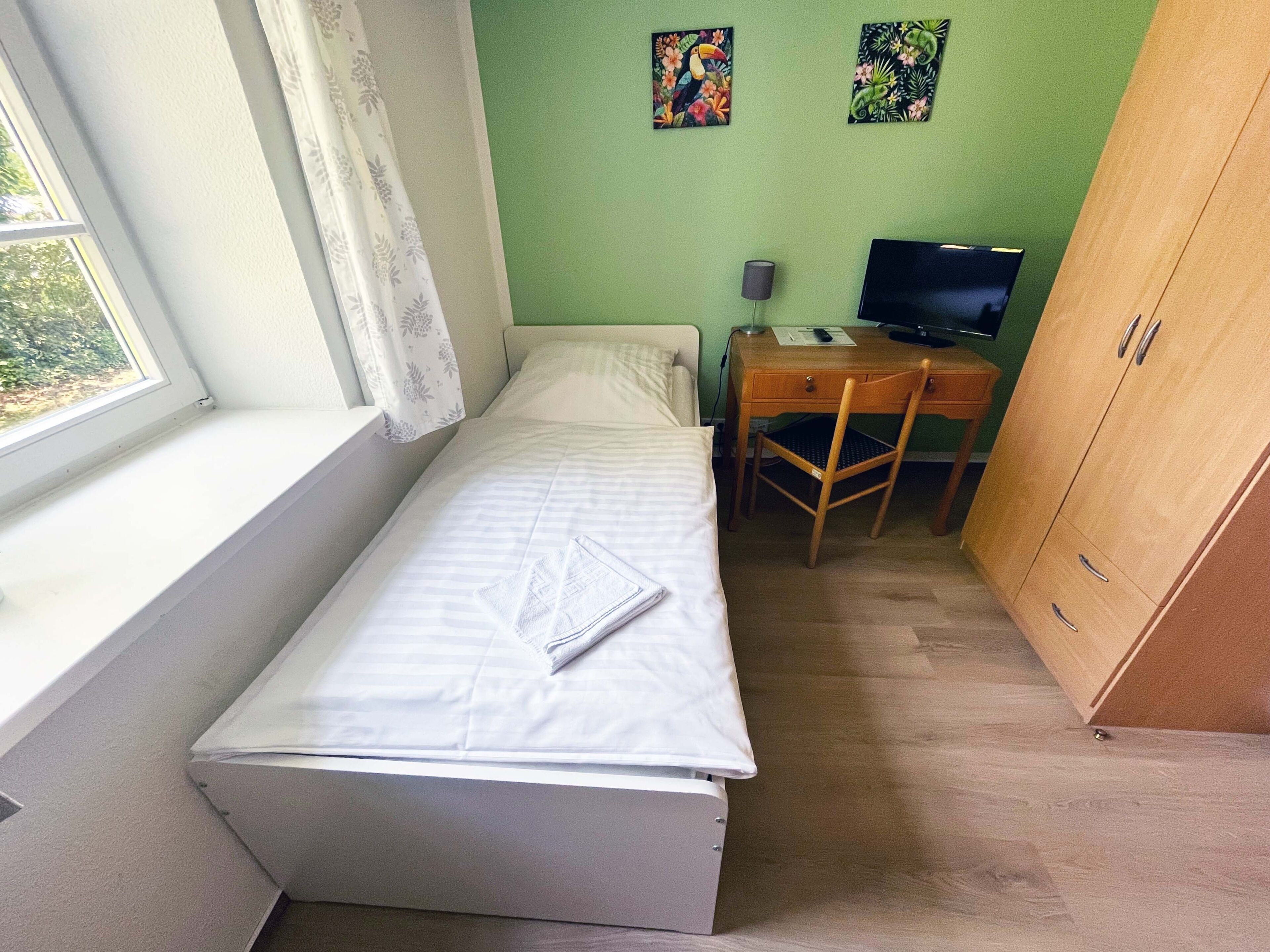 Quarto pequeno com cama de casal, escrivaninha, cadeira e guarda-roupa.
