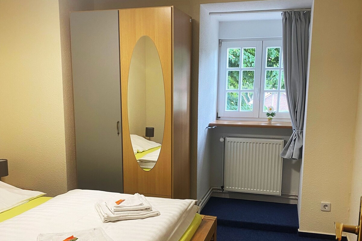 Quarto de hotel com cama, espelho, janela com cortinas e radiador.