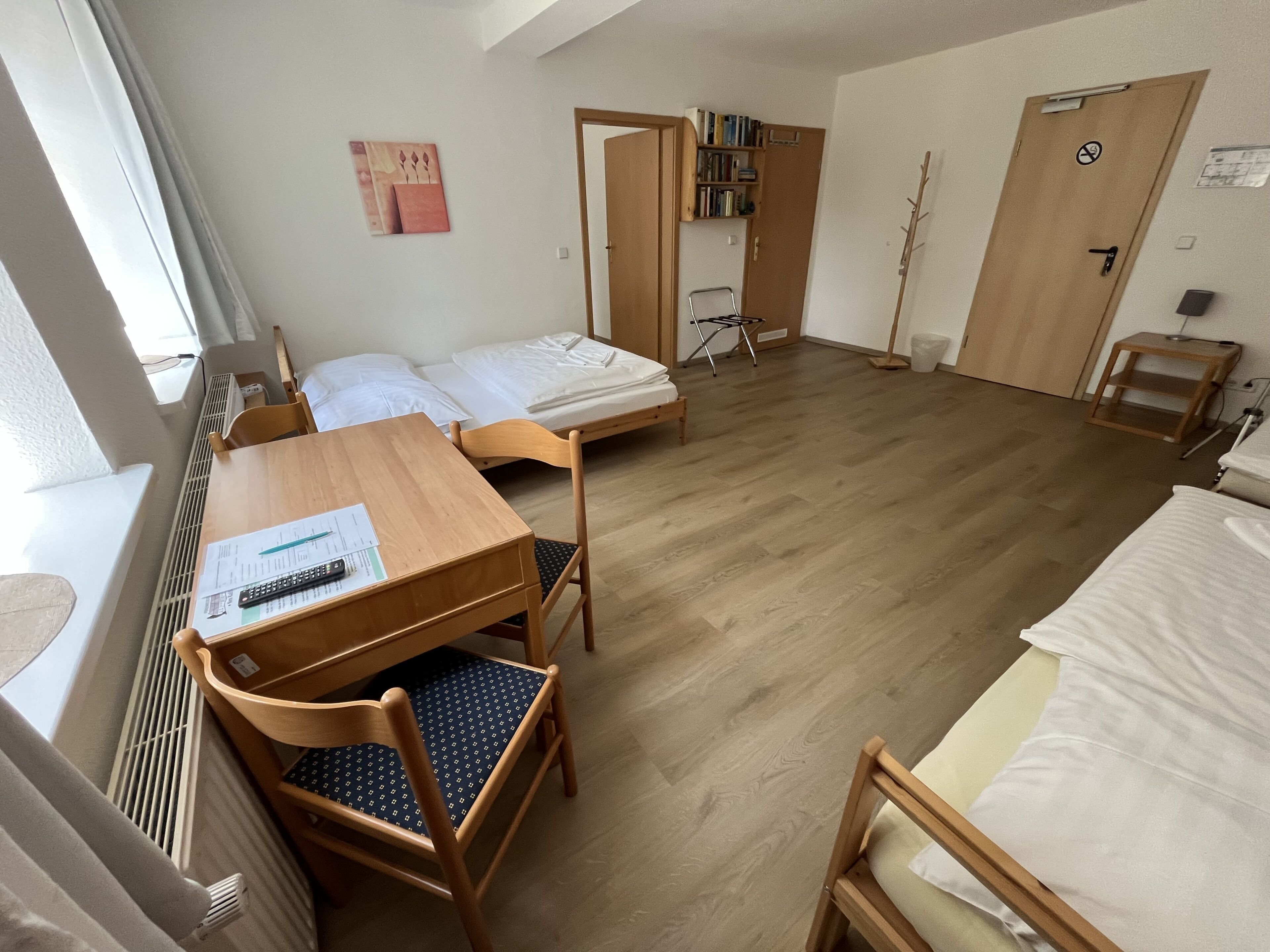 Quarto com escrivaninha de madeira, duas camas de solteiro, uma cadeira, radiador e estante.