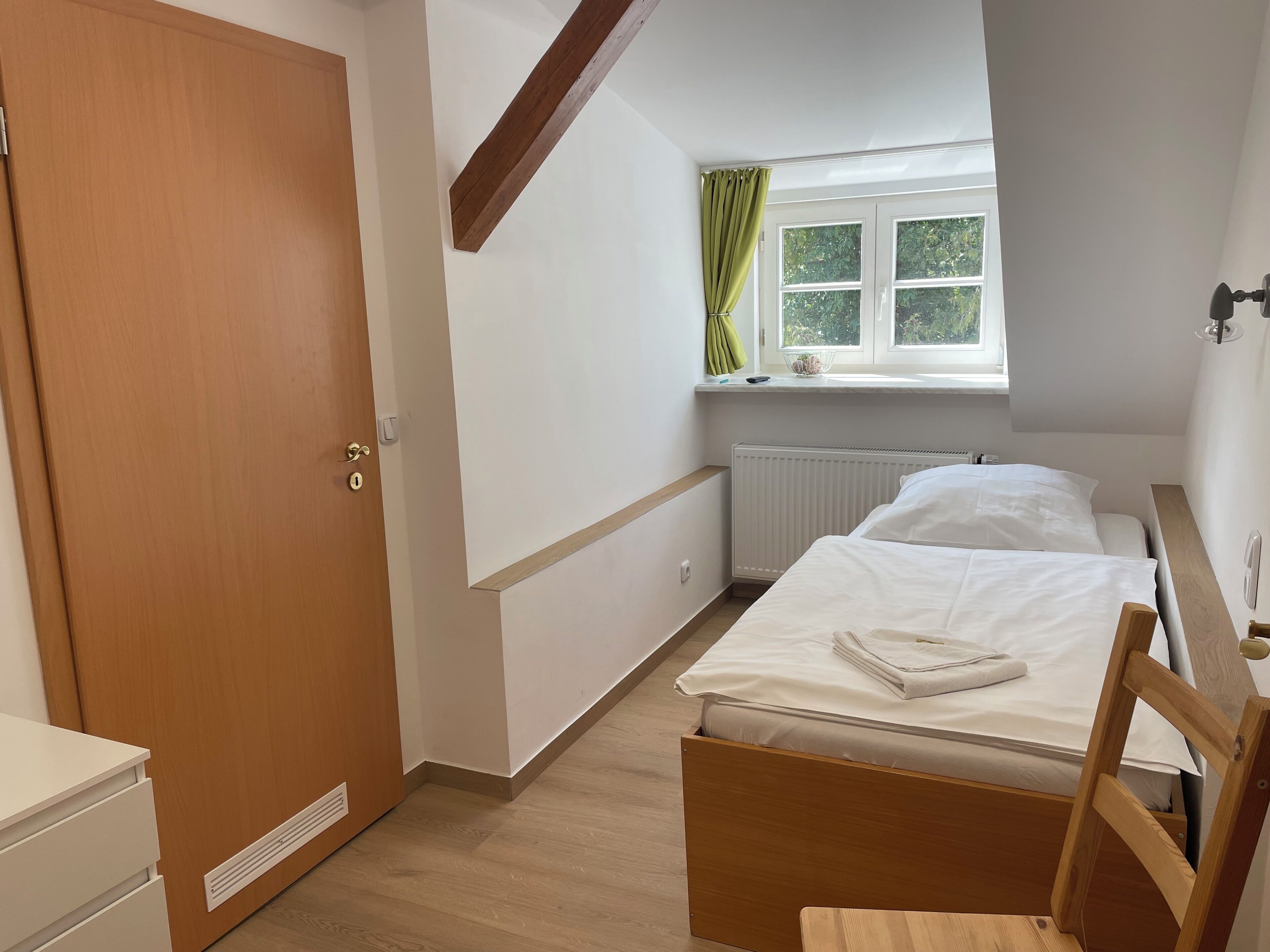 Um quarto com cama de madeira, janela com cortinas, radiador e porta de madeira.