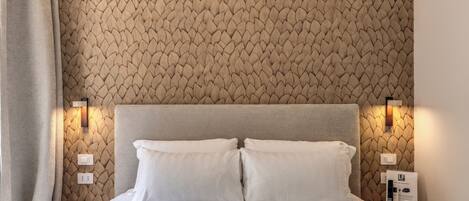 Quarto de hotel com parede estampada, duas luminárias de cabeceira, cama com roupa de cama branca e mesa de cabeceira com controle remoto.