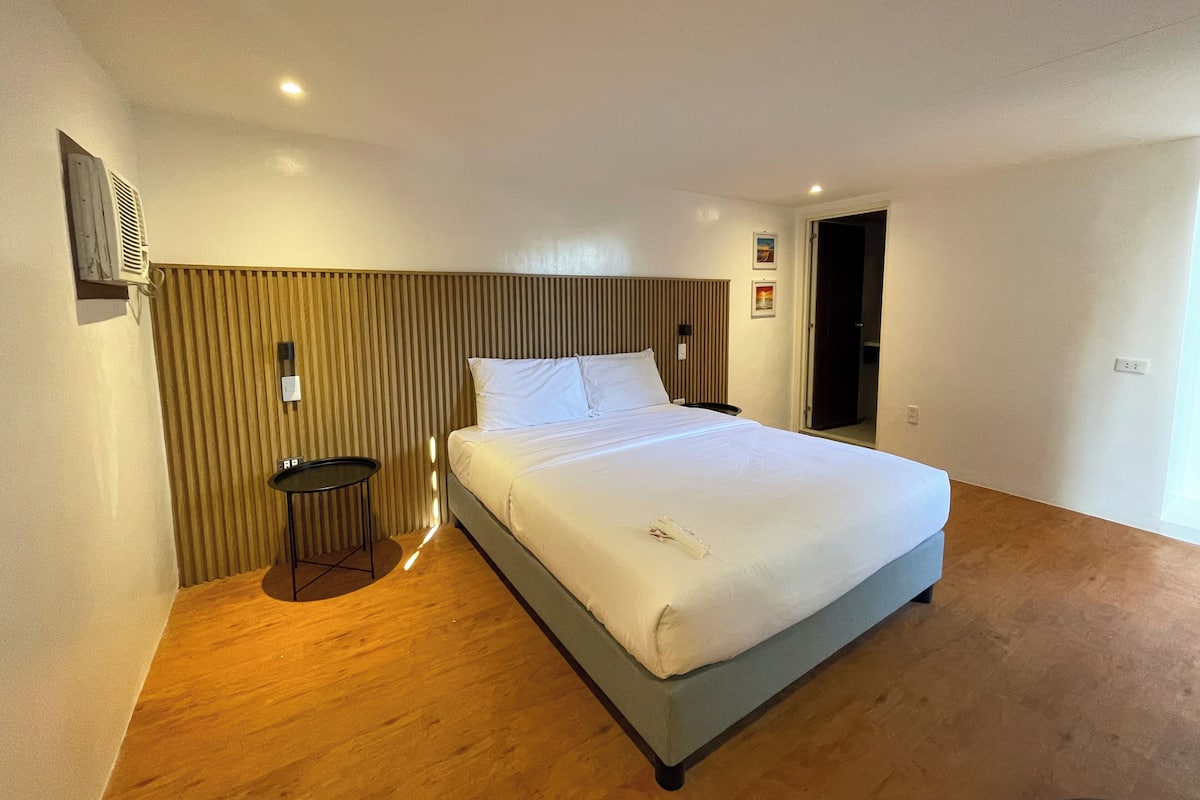 Quarto de hotel moderno com cama, mesa de cabeceira, ar condicionado fixado na parede e uma porta.