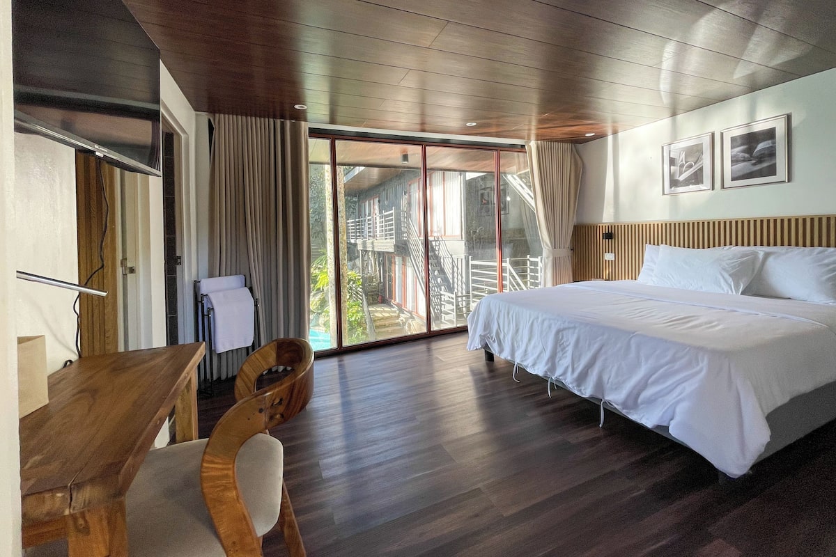 Quarto de hotel com uma cama, móveis de madeira, uma escrivaninha e vista para uma varanda.