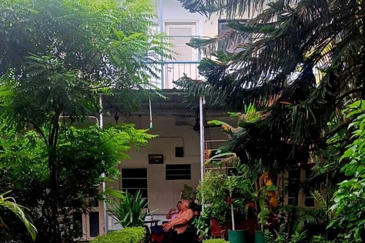 Uma trilha cercada por vegetação, conduzindo a um edifício com telhado plano e janelas.