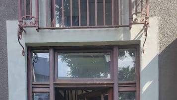 Entrada de um edifício com porta de madeira, varanda com grades de metal e um pequeno gramado na frente.