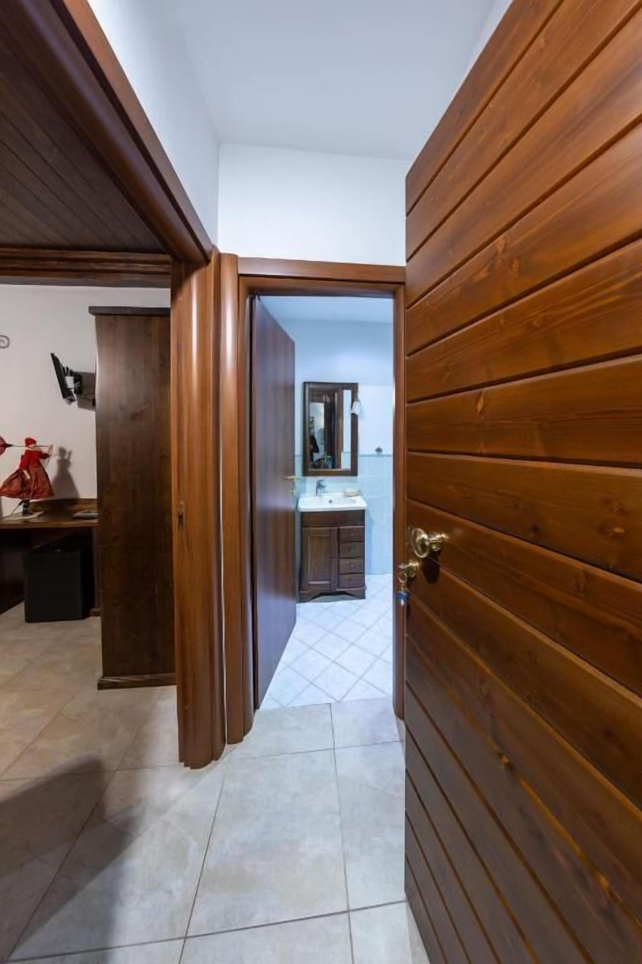 Corredor que dá para um banheiro, com porta de madeira, chão ladrilhado e pia à vista.