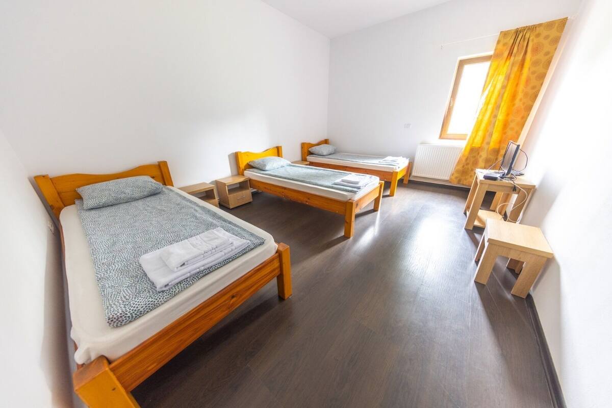 Quarto com três camas de madeira, uma mesa pequena e um radiador.