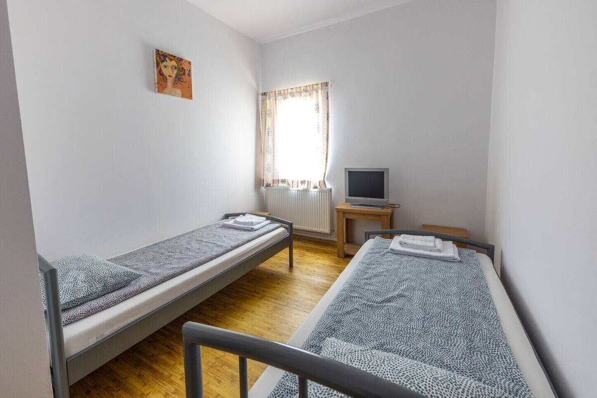 Quarto com duas camas de solteiro, uma mesa pequena com televisão e um radiador.