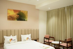 Quarto de hotel com cama, duas almofadas, cabeceira, quadro, cortina e duas cadeiras.