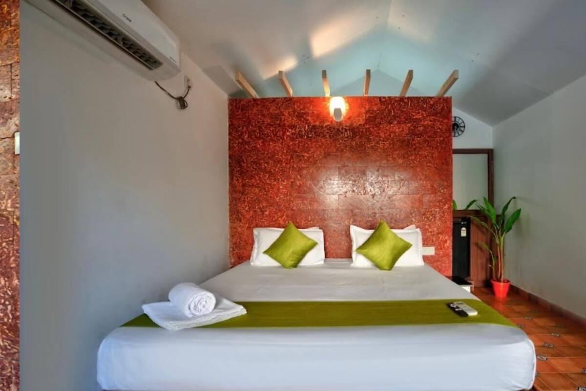 Quarto de hotel com cama, ar condicionado fixado na parede, relógio e planta em vaso.