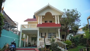 Uma casa de dois andares com telhado de telhas vermelhas, varanda e jardim frontal.