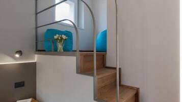Uma escadaria moderna com corrimão de metal, uma pequena mesa com uma revista e uma almofada azul ao fundo.