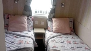 Quarto pequeno e estreito com duas camas, cada uma com travesseiro e cobre decorada.