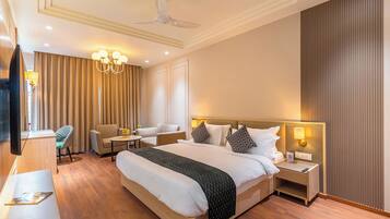 Quarto de hotel com uma cama grande, mesas de cabeceira, uma escrivaninha, uma cadeira, uma televisão e um ventilador de teto.