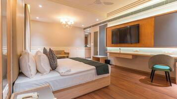 Quarto de hotel com cama, mesa de cabeceira, cadeira, escrivaninha, espelho e televisão.