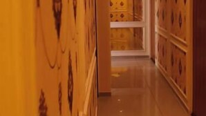 Um corredor com paredes padronizadas e piso ladrilhado, que leva a um quarto com porta estampada.