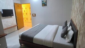 Quarto com cama, televisão, porta e quadro pendurado na parede.