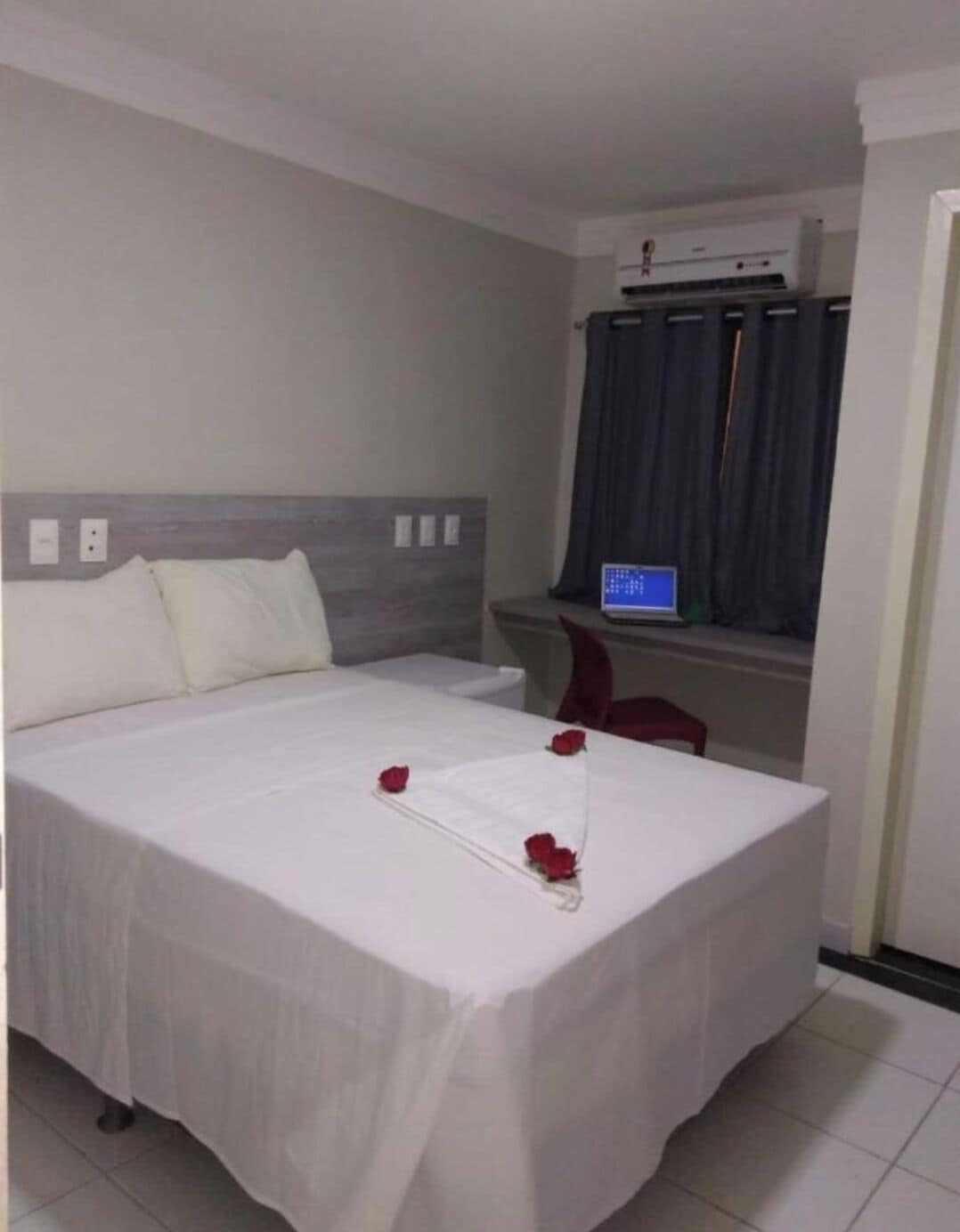 Quarto de hotel com cama, escrivaninha e janela com cortinas.