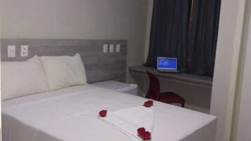Quarto de hotel com cama, escrivaninha e janela com cortinas.