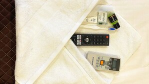 Uma cama com uma toalha branca, um controle remoto, uma garrafa de shampoo e uma garrafa de loção.