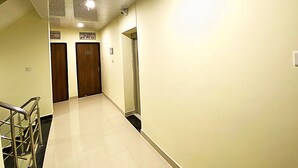 Um corredor com chão de azulejos, duas portas de madeira e um corrimão de metal.