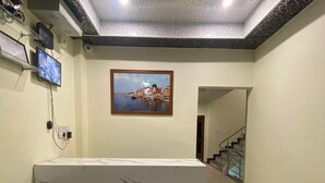 Uma área de recepção com um balcão de mármore, um sofá estampado, uma televisão montada na parede e um quadro emoldurado.