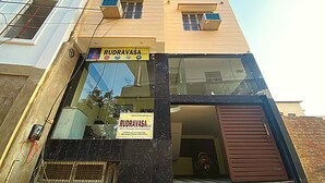Um edifício de vários andares com uma placa indicando 'RUDRAVASA Inn', que oferece quartos, um restaurante e um dormitório.