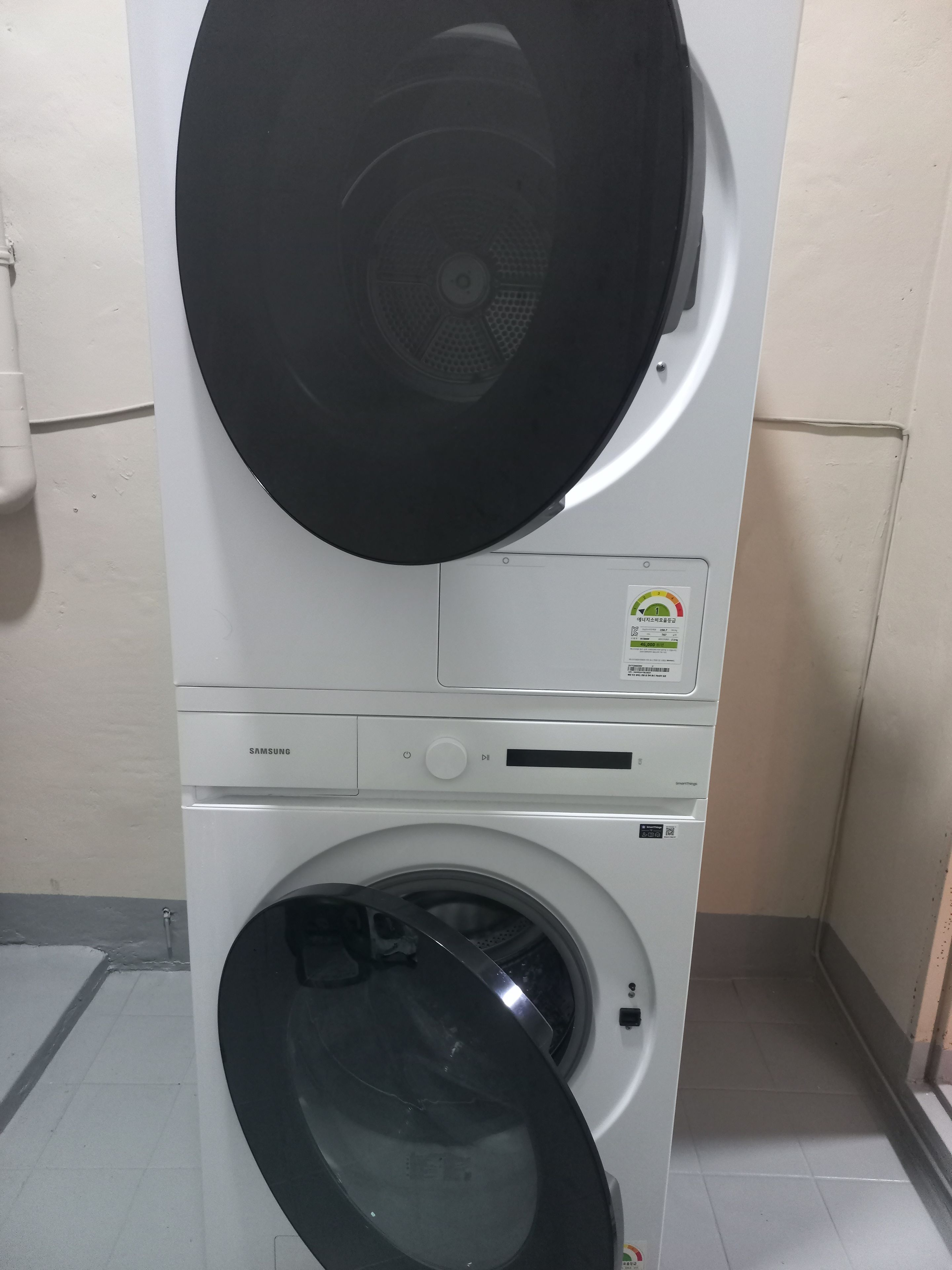Máquina de lavar e secar empilhada, com painel de controle e etiqueta de segurança.