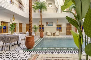 Uma área de piscina com piso ladrilhado, espreguiçadeiras e um espaço de refeições com mesas e cadeiras.