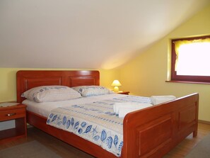 Quarto com cama de madeira, mesa de cabeceira, abajur e janela com cortinas.
