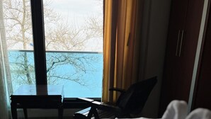 Quarto com cama, escrivaninha e vista para árvores e água lá fora.