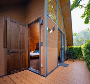 Fachada de madeira com porta deslizante que dá para um quarto com cama e mesa.